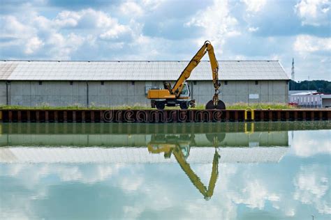 Yellow Tractor Crane Loader On The Bank Of The Canal With A Reflection In The Water Stock Image