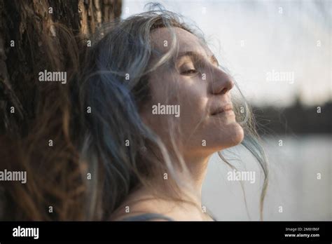 Close Up Gray Hair Woman With Half Closed Eyes Leaning Against Tree