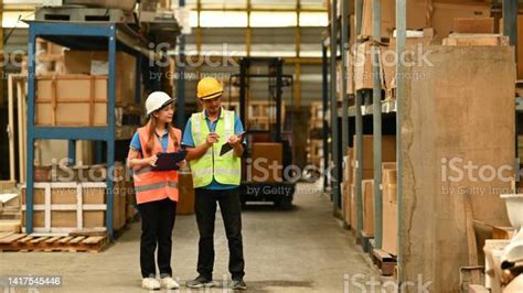 백그라운드에 골판지 상자로 가득 찬 선반이있는 창고에서 재고를 확인하는 여성 관리자와 근로자의 전체 길이 25 29세에 대한