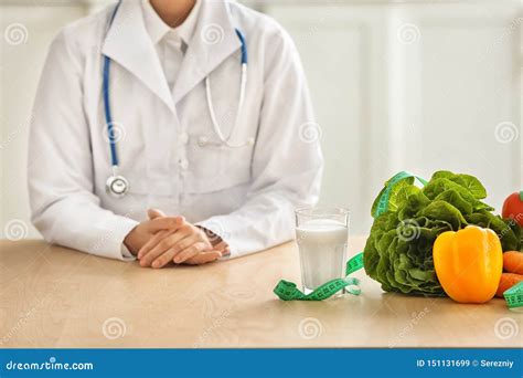 Nutricionista De Sexo Femenino Que Se Sienta En La Tabla Con Las Verduras Y El Vidrio De Leche