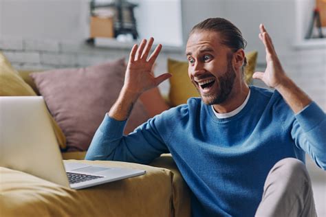 놀란 청년이 노트북을보고 집에서 바닥에 앉아있는 동안 몸짓을하면서 가정 생활에 대한 스톡 사진 및 기타 이미지 가정 생활 거실 긍정적인 감정 표현 Istock
