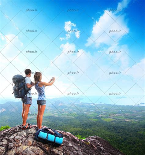 عکس با کیفیت زن و مرد گردشگر ایستاده بر روی کوه و در حال عکاسی از منظره