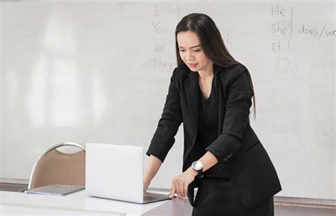 교실에서 현대 언어를 가르치는 디지털 태블릿과 노트북과 검은 비즈니스 정장 유니폼을 입고 자신감 쾌활한 아시아 여성 교사의 스톡