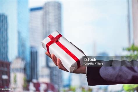 빨간 리본과 하트가 달린 하얀 선물 상자를 손에 들고 있는 한 남자가 도시 고층 빌딩을 배경으로 하고 있었다 발렌타인 밸런타인데이에 대한 스톡 사진 및 기타 이미지 Istock