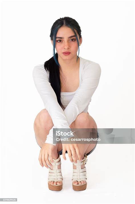 염색 한 푸른 머리와 포니 테일을 한 아름 다운 젊은 여자의 초상화 긴 소매 크롭 탑 짧은 청바지와 하이힐을 입고 흰색 배경에 무릎을 꿇고 있습니다 18 19세에 대한 스톡