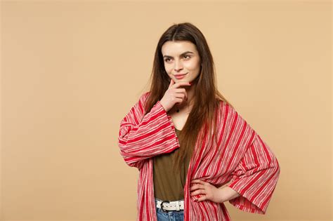 옷을 입고 웃는 젊은 여자의 초상화 옆을 보고 스튜디오에서 파스텔 베이 지 배경에 고립 된 턱에 손을 소품을 넣어 사람들은 진심으로 감정 라이프 스타일 개념입니다 복사