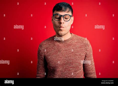 Young Handsome Hispanic Man Wearing Nerd Glasses Over Red Background Making Fish Face With Lips