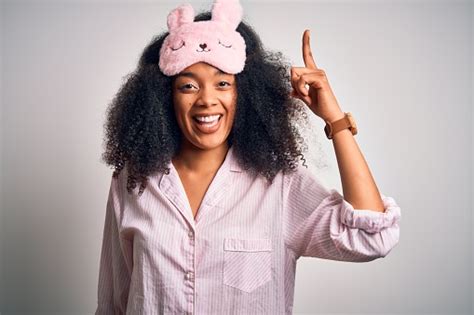 잠자는 눈 마스크와 분홍색 잠옷을 입고 아프로 머리를 가진 젊은 아프리카 계 미국인 여성은 성공적인 아이디어로 손가락을 가리킵니다 종료하고 행복 넘버 원 가리키기에 대한