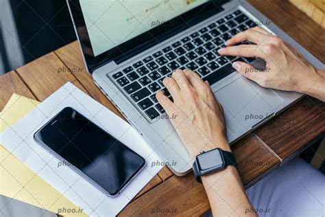 عکس مرد در حال کار با لپ تاپ روی میز چوبی در کنار گوشی هوشمند عکس با کیفیت و تصاویر استوک حرفه ای