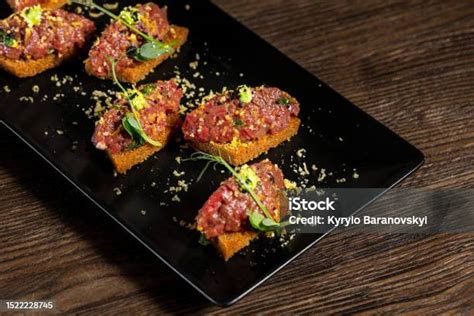 마이크로그린과 아보카도 한 조각으로 장식된 비프 타르타르에 마늘 버터에 볶은 구운 메밀 빵을 얹은 요리 음식은 나무 배경에 직사각형 세라믹 접시 위에 놓여 있습니다 0명에