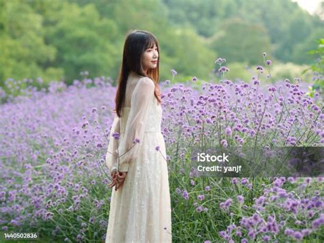 보라색 버베나 보나리엔시스 꽃밭 사이에서 포즈를 취하는 흰색 드레스를 입은 아름다운 여성 검은 긴 머리를 가진 매력적인 중국 소녀는 야외에서 여가 시간을 즐깁니다 꽃 식물에