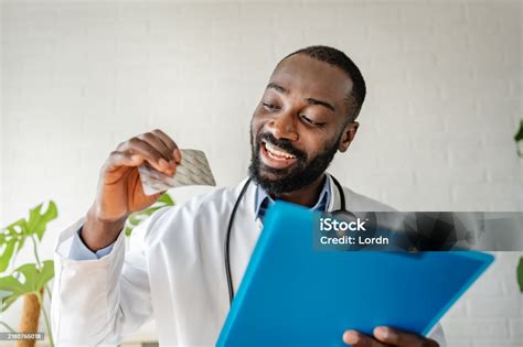 한 아프리카계 미국인 의사가 알약이 든 물집 팩과 클립보드를 들고 온라인 상담 중에 약물 복용 지침을 설명하고 있다 그는 전문적이고 세심한 것처럼 보입니다 건강 진단에 대한