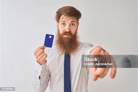 카메라와 당신에 게 손가락으로 가리키는 고립 된 흰색 배경 위에 서 신용 카드를 들고 젊은 빨간 머리 아일랜드어 사업가 손 기호