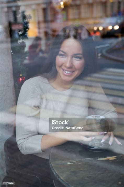 한 아름다운 소녀가 카페에 앉아 창 밖으로 신중하게 보입니다 창에서 도시의 반사 긴 머리 음료 카푸치노 커피 수직으로 웃는 갈색 머리 여자 가을에 대한 스톡 사진 및 기타