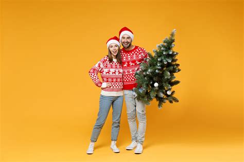 전체 크기의 길이 웃음 젊은 산타 커플 친구 남자 여자 입고 빨간 스웨터 크리스마스 모자 포옹 개최 전나무 나무 고립 노란색 배경 스튜디오에 고립 새해 복 많은 연말연시