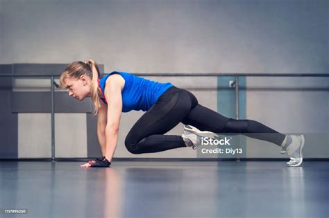 매력적인 젊은 여성이 실내에서 일하고 있습니다 흰색 벽과 함께 방에서 운동을 하 고 아름 다운 모델 블랙 레 깅 스 블루 T 셔츠에 금발 다리의 굽 힘과 확장 운동 다리