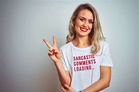 아름다운 여성은 승리 표지판을하고 카메라에 윙크 행복한 얼굴로 미소 고립 된 배경 에 티셔츠를로드 Sacarstic 코멘트를