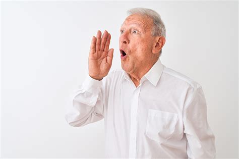 고립 된 흰색 배경 위에 서있는 우아한 셔츠를 입은 선임 회색 머리의 남자가 입에 손을 대고 큰 소리로 외치고 비명을 지르고