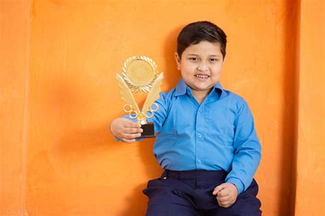 트로피를 보여주거나 승리를 축하하는 교복을 입은 행복하고 사랑스러운 귀여운 인도 소년의 초상화 주황색 배경 기술 인도를 배경으로
