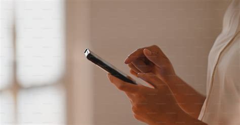 하얀 셔츠를 입은 아름다운 사업가가 현대적인 미니멀 거실을 배경으로 스마트폰을 손에 들고 인터넷을 서핑하는 모습 사진