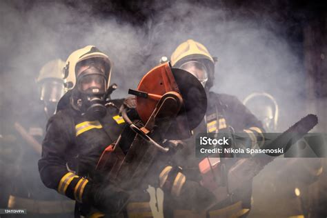전체 장비 산소 마스크 및 비상 구조 도구 원형 유압 및 가스 톱 도끼 및 썰매 망치를 착용한 전문 소방관 그룹 백그라운드에서 연기와 소방차 4 명에 대한 스톡 사진 및