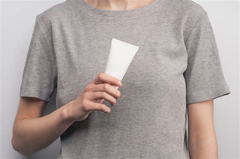 흰색 배경에 격리된 빈 흰색 화장품 튜브 크림을 바른 여성의 손이 화장품 튜브에 닿습니다 크림 핸드 로션의 개념 겨울 피부 관리 튜브에서 핸드 크림을 사용하는 여자 전체