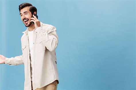 갈색 머리 애니메이션과 기쁨 전화로 이야기하는 기쁨 깜짝 승리와 행복 이빨로 미소 흰 티셔츠와 청바지에 파란색 배경 복사 공간의 손을 손을 내밀고 25 29세에 대한 스톡