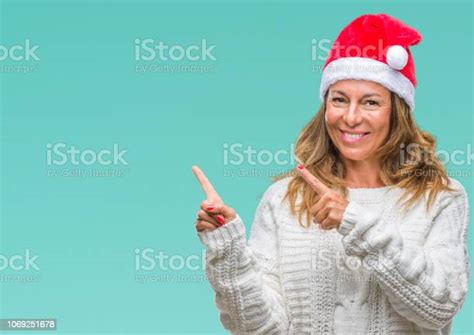 중 년 수석 히스패닉 여자 웃 고 옆에 두 손과 손가락으로 가리키는 카메라 보고 격리 된 배경 위에 크리스마스 모자를 쓰고 가리키기에 대한 스톡 사진 및 기타 이미지