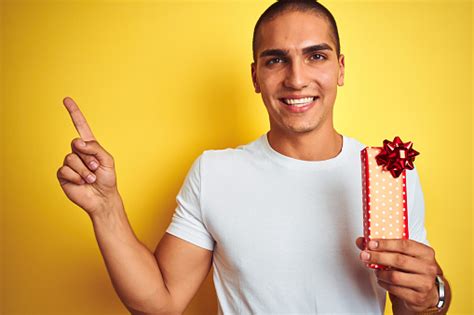젊은 백인 남자 들고 생일 선물 위에 노란색 고립 된 배경 매우 행복 가리키는 손과 손가락 으로 측면에 가리키기에 대한 스톡 사진 및 기타 이미지 Istock