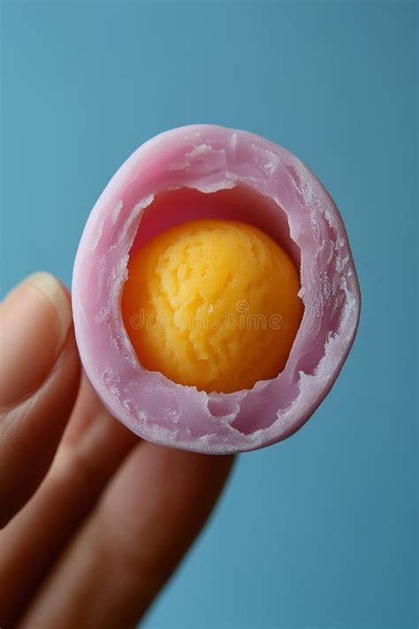 A Hand Holds A Pink Mochi Filled With White Cream The Mochi Is Split Open Showing Yellow