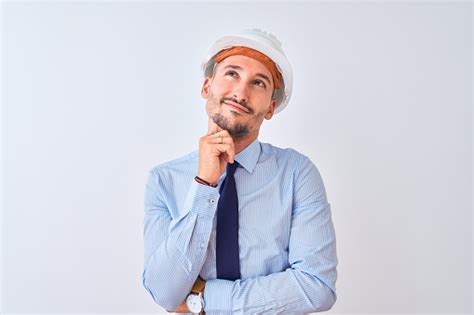 고립 된 배경 위에 계약자 안전 헬멧을 쓰고 있는 젊은 사업가가 턱에 손을 얹고 질문 펜시브 표현을 생각하고 있습니다 사려 깊은 얼굴로 미소 의심 개념 건축가에 대한 스톡