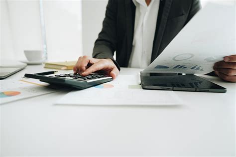 사업가 또는 회계사는 사무실에서 회계 문서를 사용하는 동안 비즈니스 데이터를 계산하기 위해 계산기와 랩톱 컴퓨터에서 작업합니다