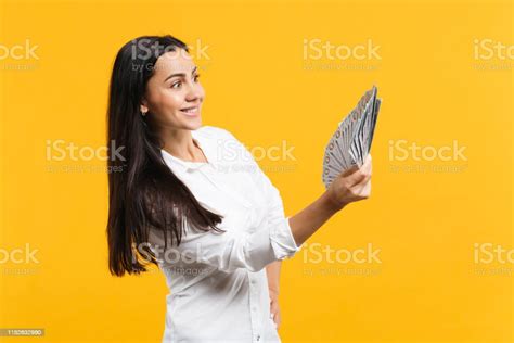 스튜디오에서 노란색 오렌지 벽 배경에 고립 달러 지폐 현금 돈의 팬을 들고 흰색 캐주얼 셔츠에 웃는 젊은 여자의 초상화 사람들 라이프 스타일 개념입니다 복사 공간을 모의