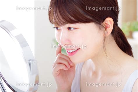 鏡を見ながら顔のスキンケアをする若い女性の写真素材 イメージマート