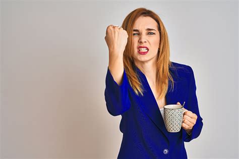 빨간 머리 백인 비즈니스 여자 고립 된 배경 을 통해 커피 한 잔을 마시는 짜증나고 좌절 된 분노와 함께 소리 미친 고함 제기 손으로 분노 개념 감정에 대한 스톡 사진 및