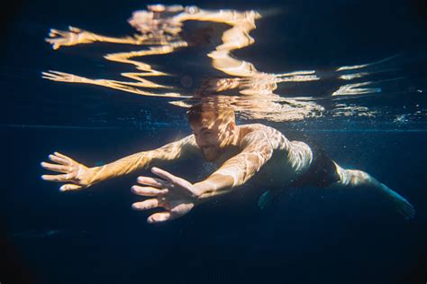 A Handsome Young Man Swims Underwater In A Swimming Pool While On