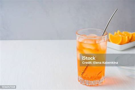 신선한 오렌지 스파클링 주스는 빨대 얼음 조각 흰 나무 배경에 얇게 썬 감귤류와 함께 키가 큰 마시는 유리에 제공됩니다 칵테일에