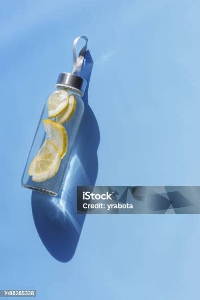 레몬 물이 담긴 유리병은 파란색 배경에 햇빛을 받아 해독을 한다 건강한 천연 주입 물은 신진 대사와 체중 감소를 촉진합니다 미적 정물 상쾌한 여름 음료 개념에 대한 스톡