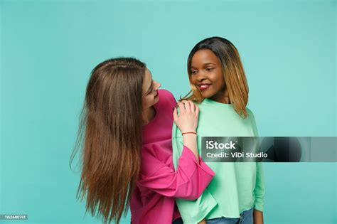 두 젊은 여자 친구 파란색 청록색 벽 배경 스튜디오 초상화에 고립 된 포즈를 서 있는 분홍색 녹색 옷에 유럽과 아프리카계 미국인