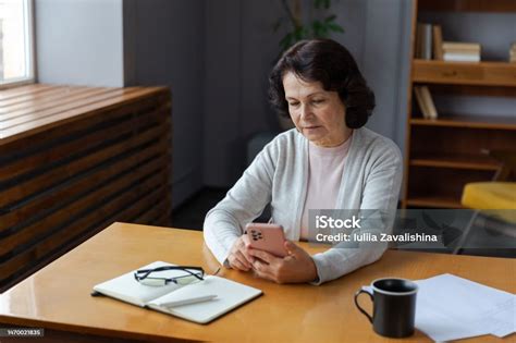 유럽 중년 노인 여성이 스마트폰 터치 스크린 타이핑 스크롤 페이지를 사용하여 들고 있습니다 세련된 나이든 성숙한 60대 숙녀는 집에서 인터넷 소셜 미디어 앱을 사용하여