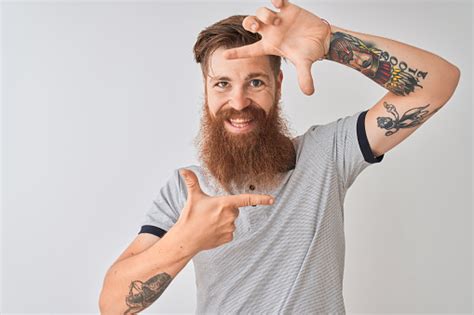 행복한 얼굴로 손과 손가락으로 프레임을 만드는 고립 된 흰색 배경 위에 서있는 회색 폴로를 입은 젊은 빨간 머리 아일랜드 남자 창의력과 사진 개념 개념에 대한 스톡 사진 및