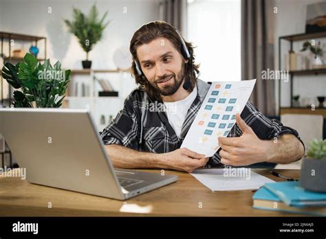 Serious Young Man In Headset Having Video Conference On Laptop While Working From Home