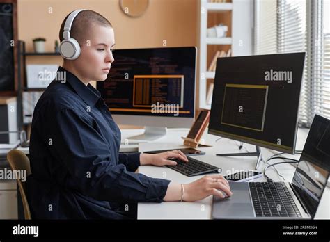 Portrait Of Female Programmer Wearing Headphones And Using Computer While Writing Code And