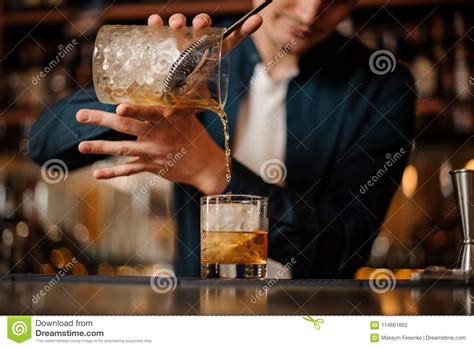 Brunet Bartender Pouring An Alcoholic Drink Into A Glass With A Big Ice