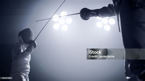 두 명의 전문 펜싱 선수가 장엄한 파란색 무대 조명과 연기 효과로 전투에서 서로 결투하는 검을 포지합니다 로우 앵글 뷰 18