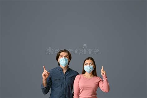 Millennial Couple Wearing Protective Medical Masks Pointing Upwards At