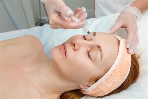 미용사는 여성의 얼굴 피부에 주름을 조이고 부드럽게하기 위해 얼굴에 젊어지게하는 주사 절차를 수행합니다 뷰티 살롱에서 화장품 스킨 케어 건강관리와 의술에 대한 스톡 사진 및