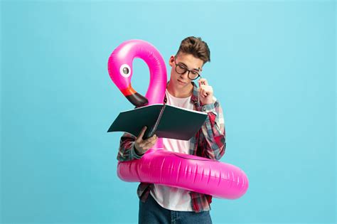 젊은 백인 남자의 절반 길이 초상화 메모장과 밝은 파란색 배경에 고립 된 수영 원을 가진 학생 플라스틱 플라밍고에 대한 스톡 사진 및 기타 이미지 Istock