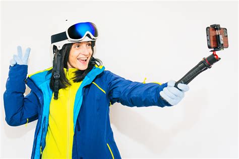 닫다 젊은 웃는 만족스러운 스키어 여자 따뜻한 패딩 처리된 윈드 브레이커 재킷 모자 스키 고글 마스크 보기 카메라 여행 휴식 주말 겨울 여름 겨울 여름 산 절연 통하고 있