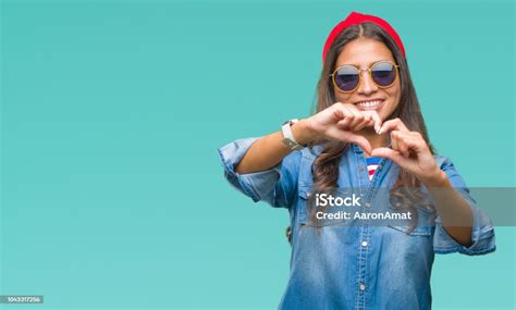 젊은 아름 다운 아랍 여자 마음 기호와 손으로 모양을 보여주는 사랑에 웃 고 고립 된 배경 위에 선글라스를 착용 낭만적인 개념입니다 개념에 대한 스톡 사진 및 기타 이미지
